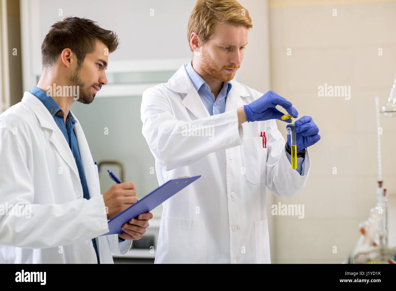 Laboratory technician mixing liquids in lab while assistant write data ...