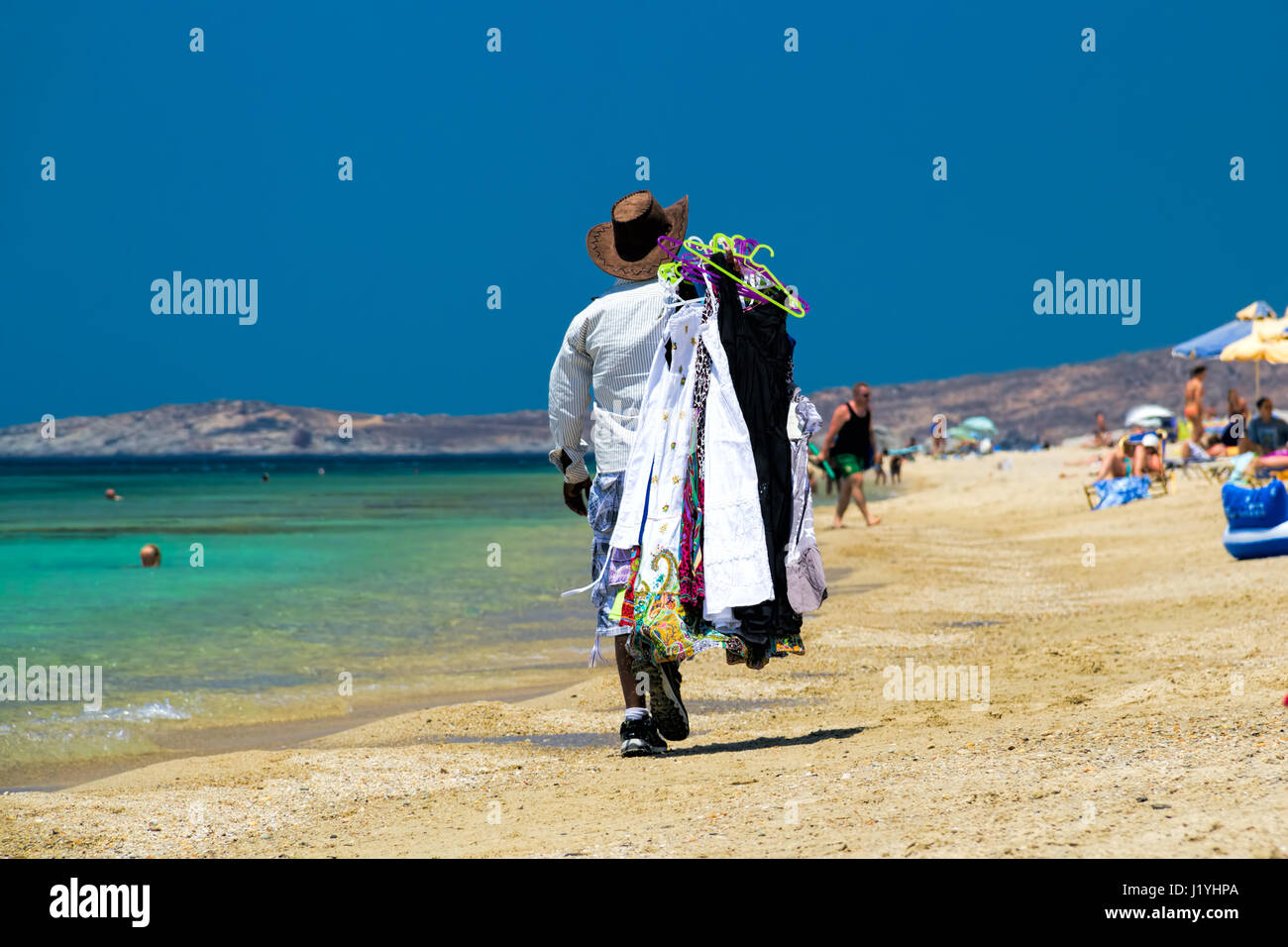 Seller on the beach - Back view of a man walking along the beach ...