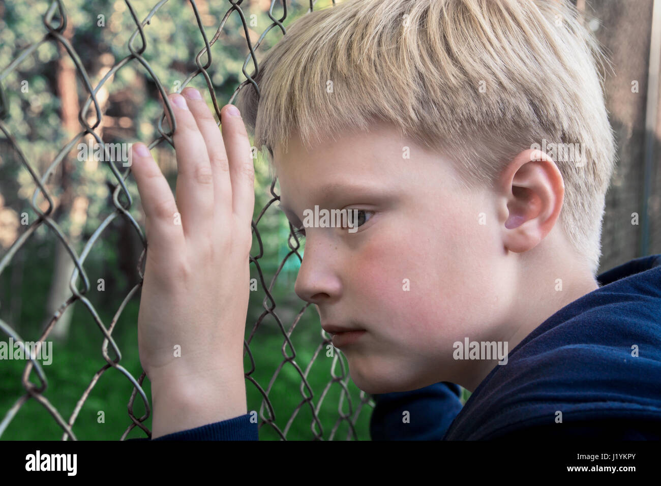 Sad, upset, frustrated boy (child, kid, teen) near metal mesh, close up ...