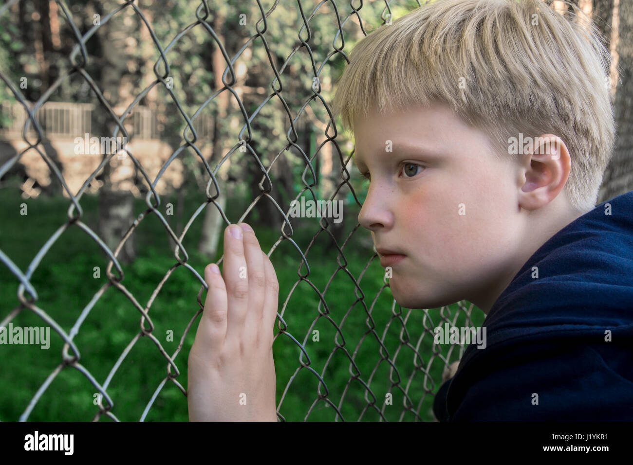 Sad, upset, frustrated boy (child, kid, teen) near metal mesh, close up ...