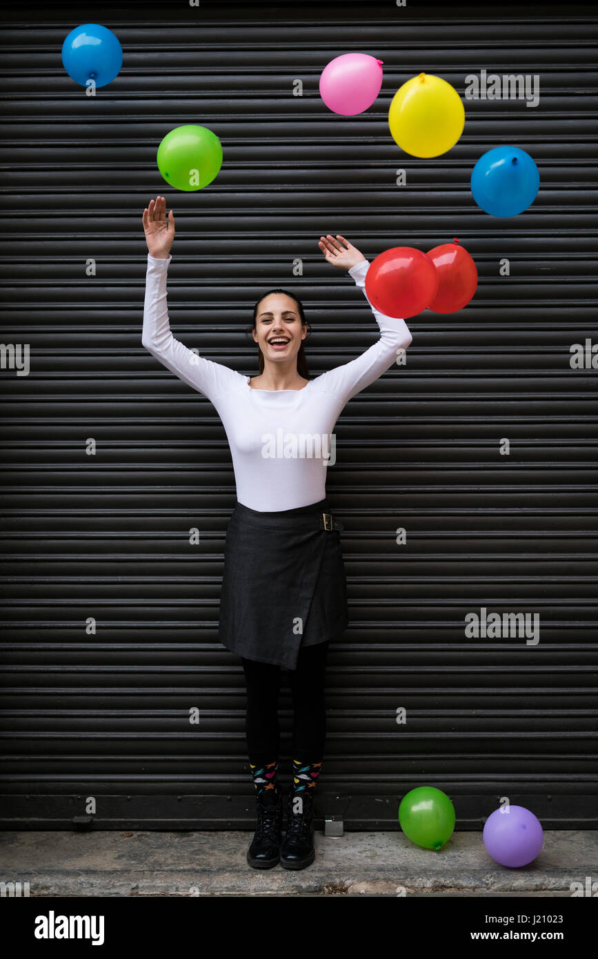Happy young woman standing in front of black roller shutter with flying ...