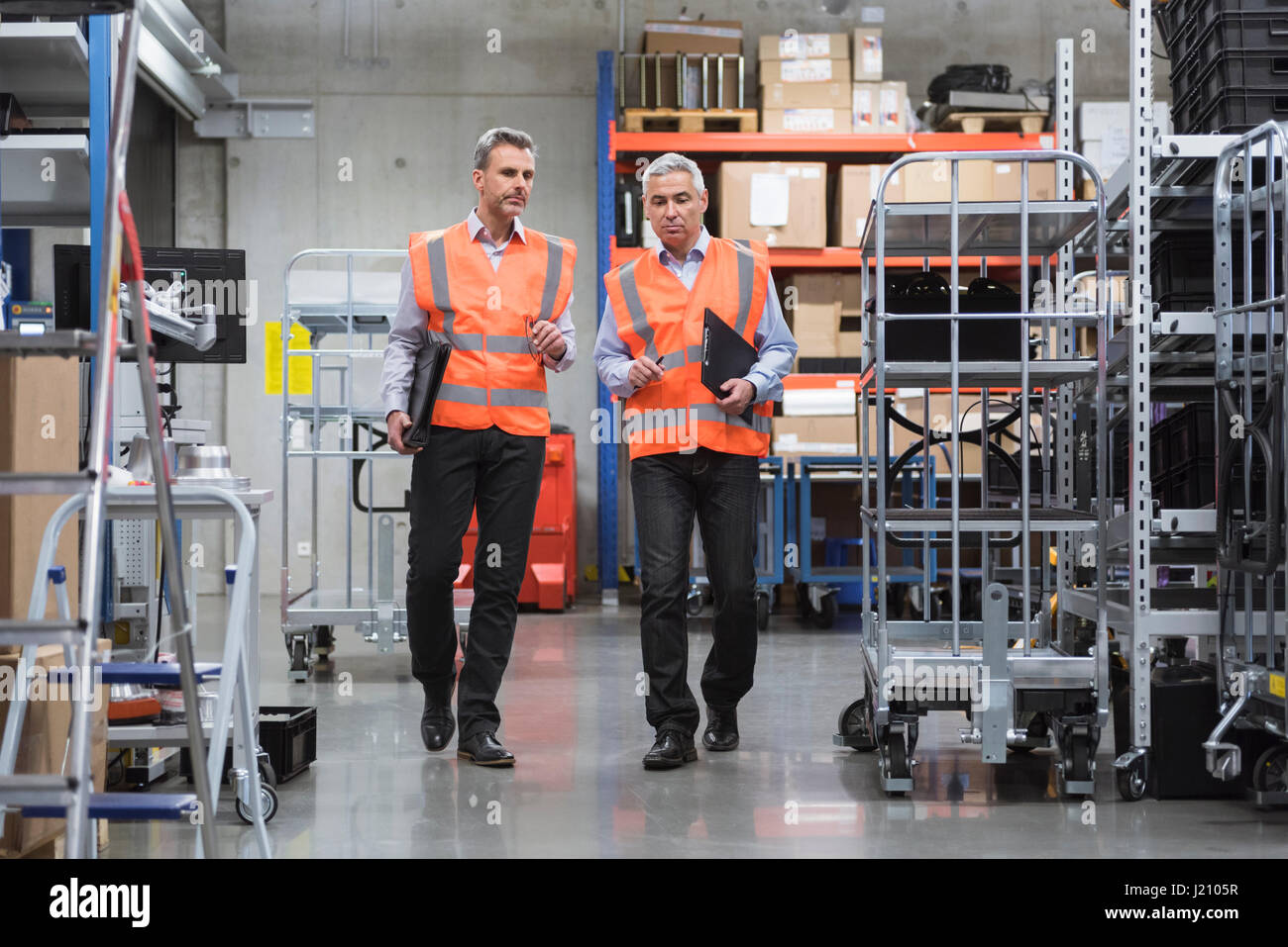 Two colleagues walking in factory hall wearing safety vests Stock Photo ...