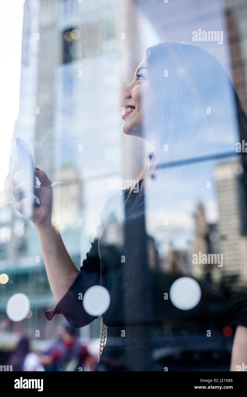 USA, New York City, Manhattan, smiling young woman behind glass pane ...