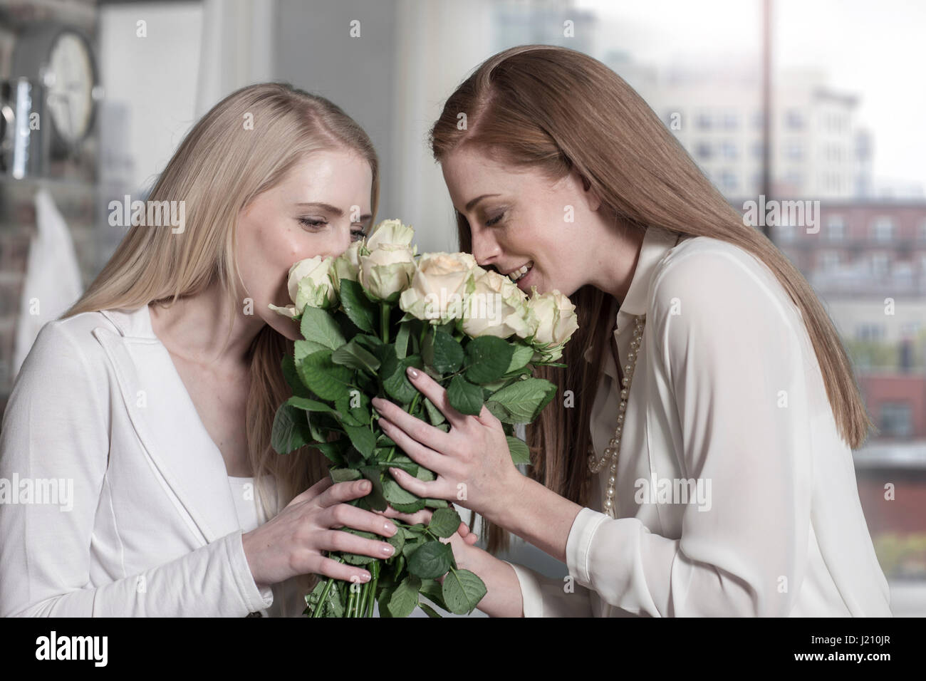 Two young women smelling roses at home Stock Photo - Alamy