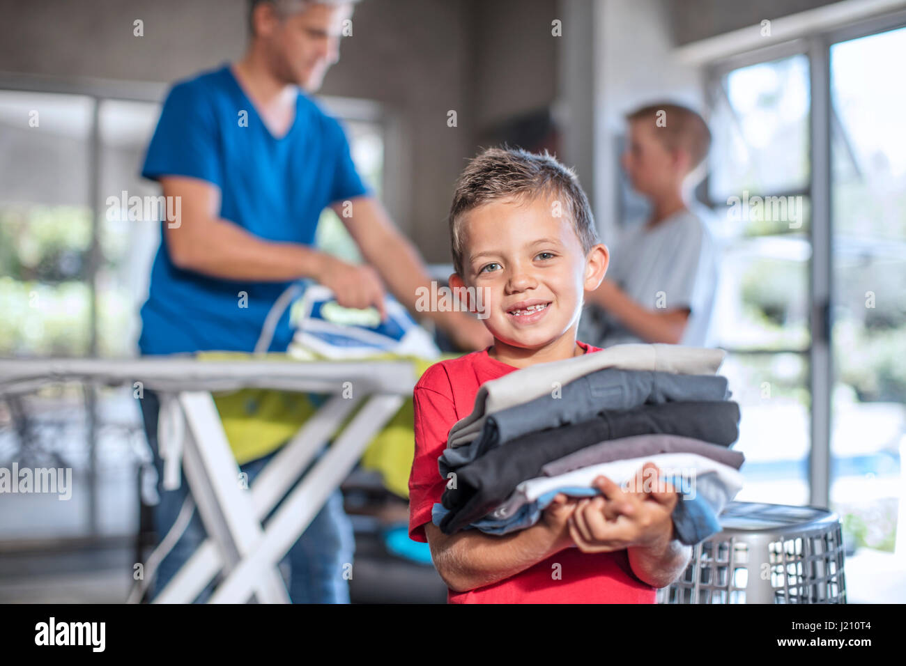 Smiling boy helping with chores holding folded clothes Stock Photo - Alamy