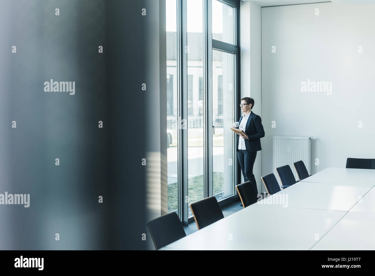 Businesswoman looking out of office window Stock Photo - Alamy