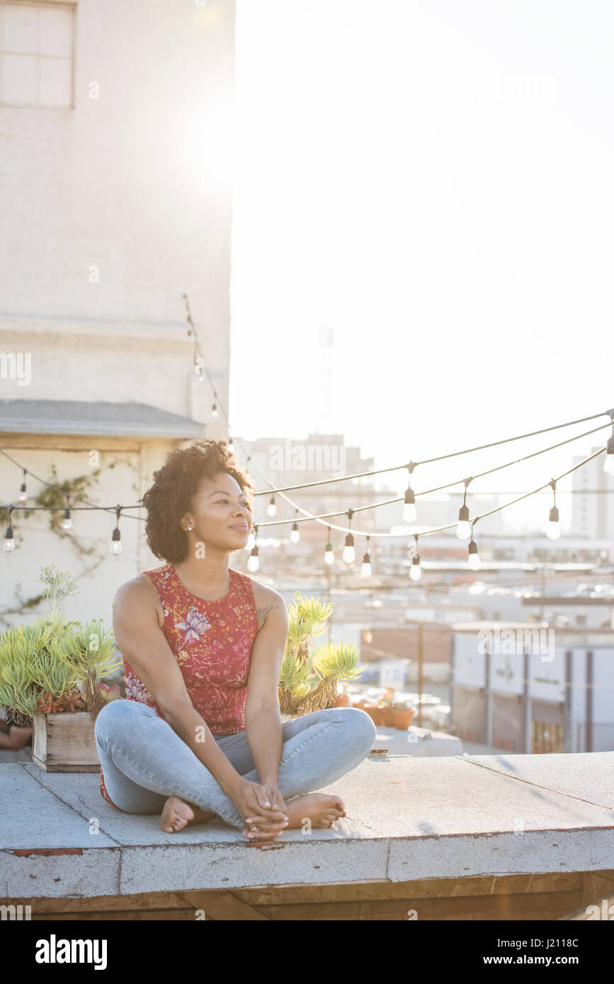 Young woman sitting on rooftop terrace, enjoying the sun Stock Photo ...