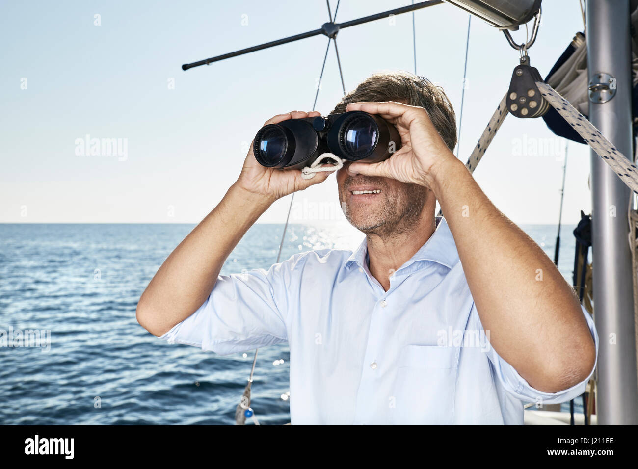 Mature man using binoculars on his sailing boat Stock Photo - Alamy