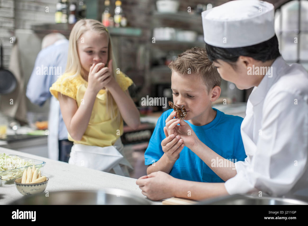 Boy and girl smelling food from female chef in cooking class Stock ...