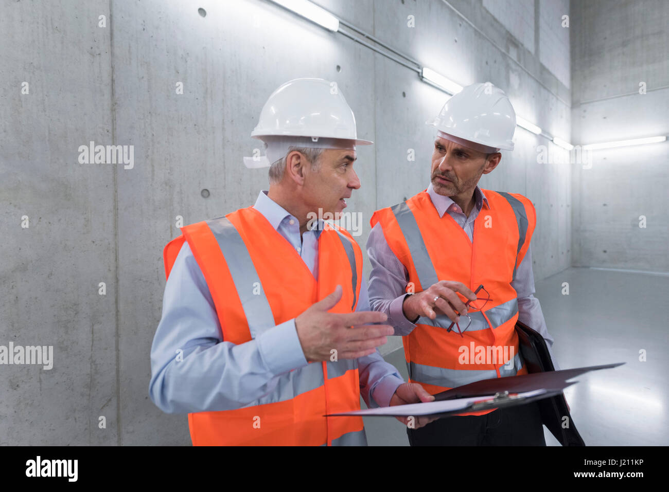Two colleagues wearing safety vests and hard hats talking in a building ...