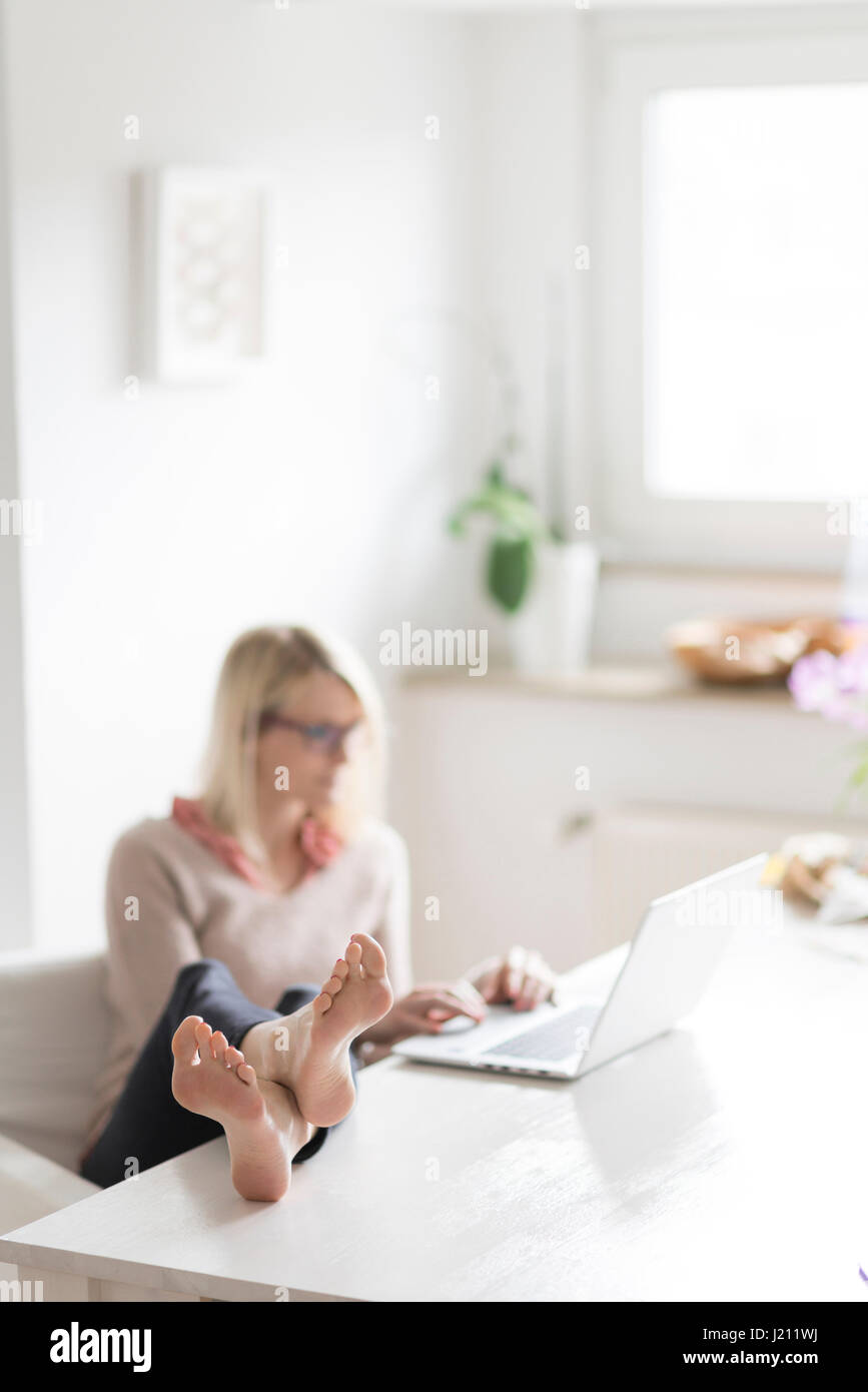 Woman sitting at table with feet up using laptop Stock Photo - Alamy