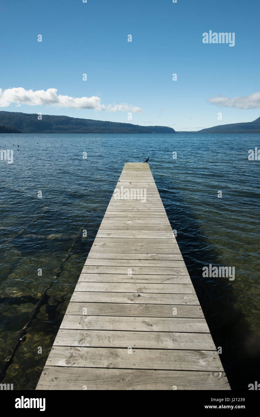 Small jetty pocking out into a lake under a clear blue sky Stock Photo ...