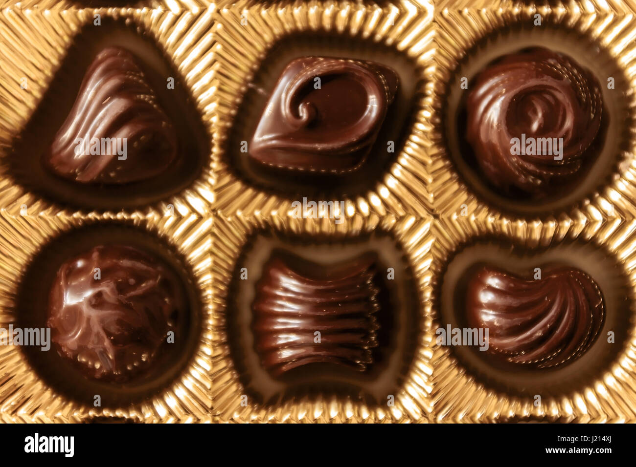 Chocolate candies of different shapes in a gold box, top view, smooth ...