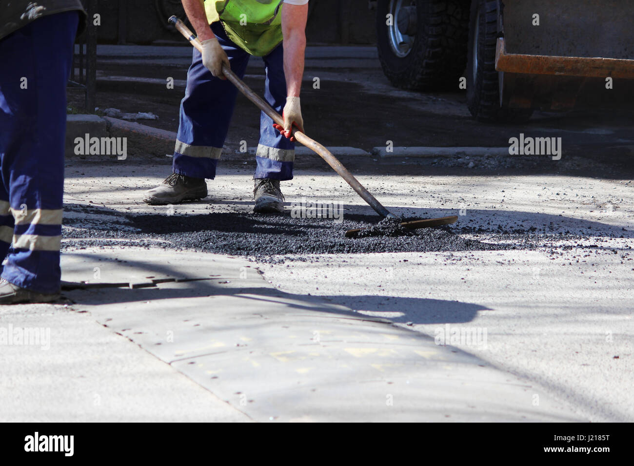 The worker is leveling the crumb of asphalt in the pit with a drag ...