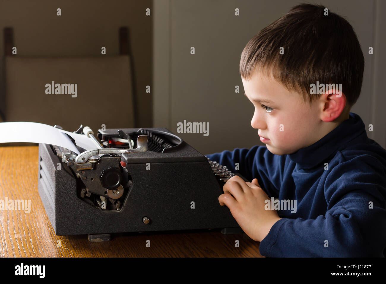 Cute little boy typing a letter on a vintage black typewriter at home ...