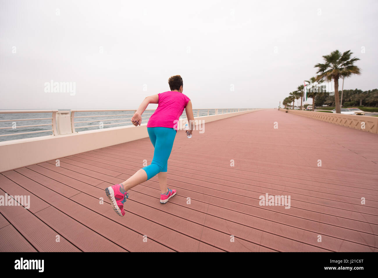 very active young beautiful woman busy running on the promenade along ...