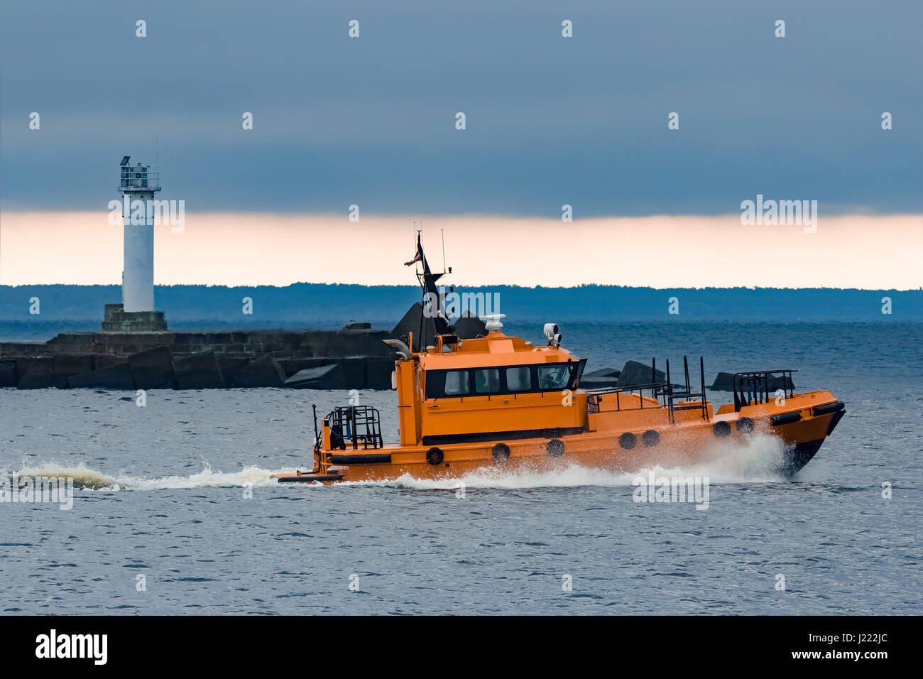 Orange pilot ship moving at speed past the lighthouse in Riga Stock ...