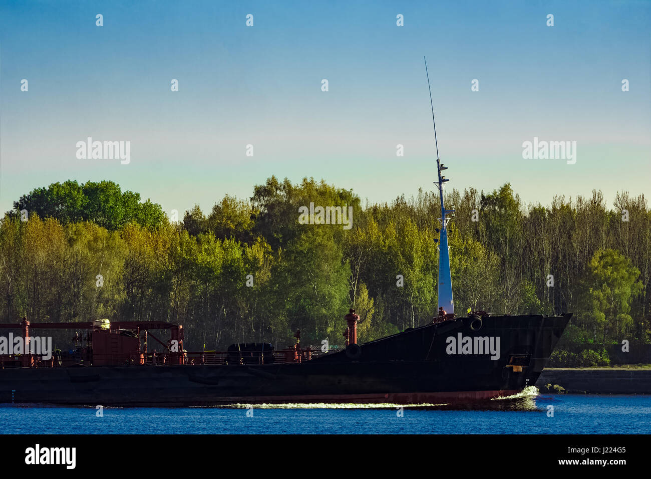 Black cargo oil tanker's bow against summer green trees Stock Photo - Alamy