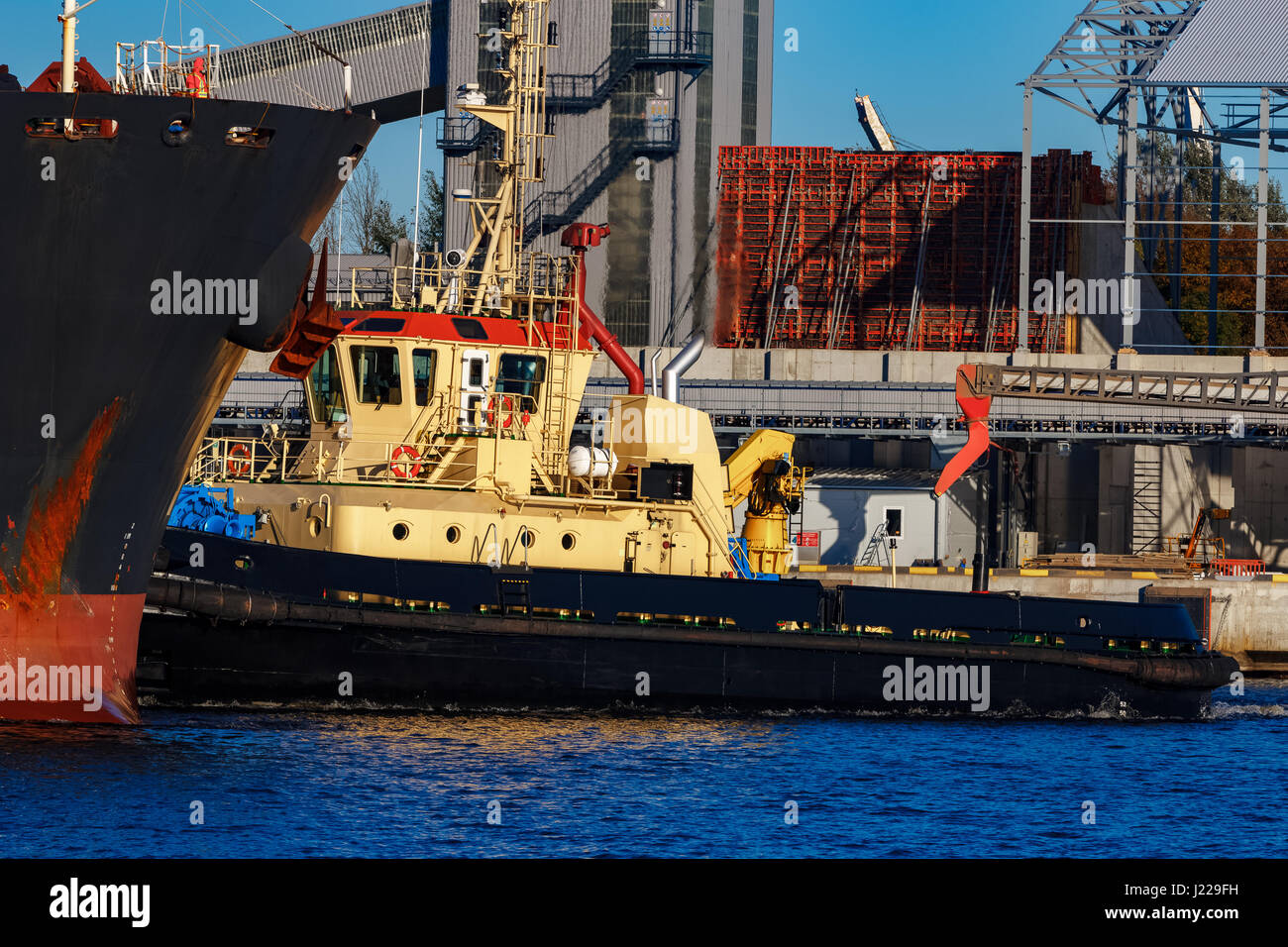 Black cargo ship mooring at the port with tug ship support Stock Photo ...