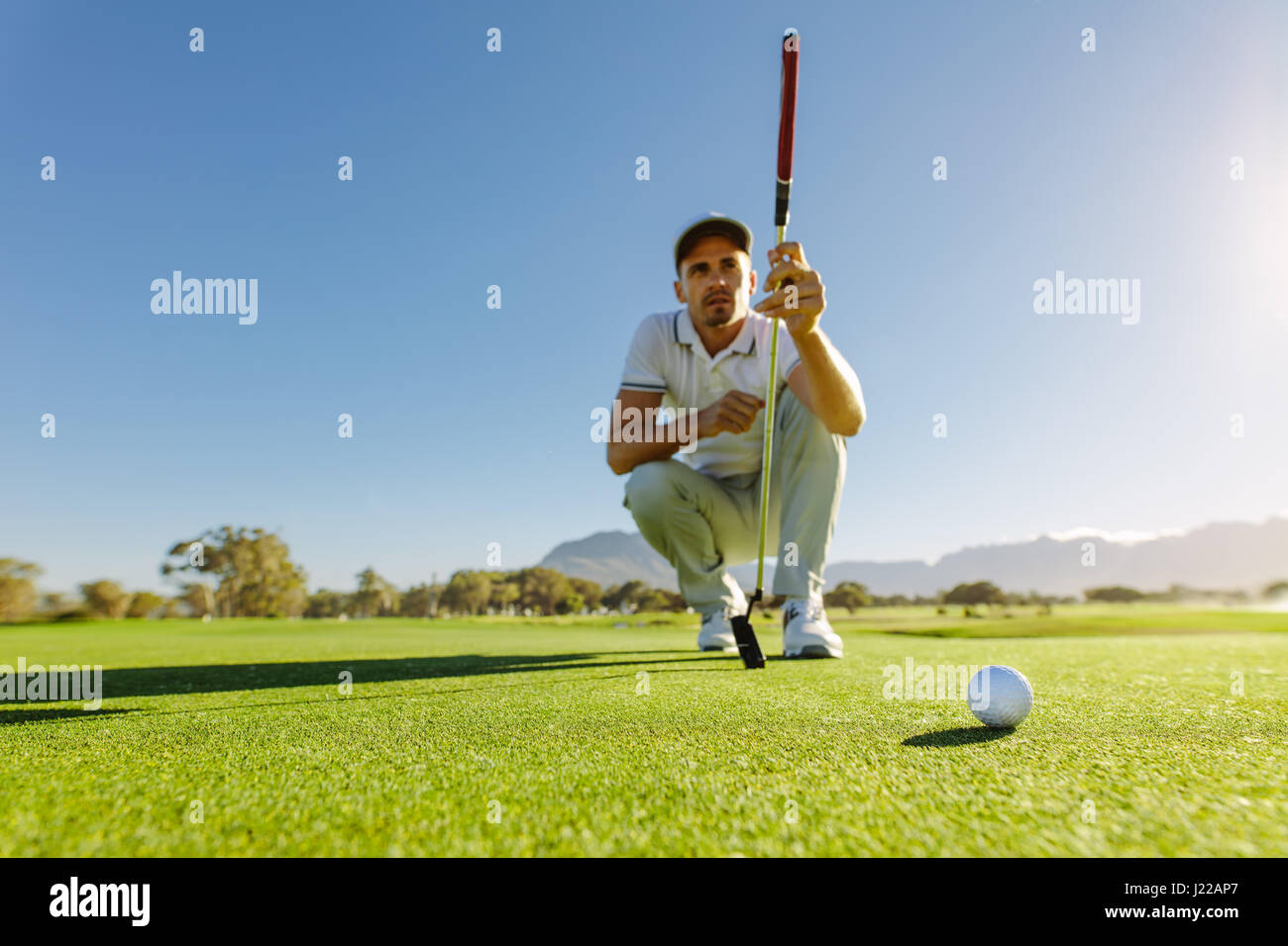 Pro golf player aiming shot with club on course. Golfer crouching and ...
