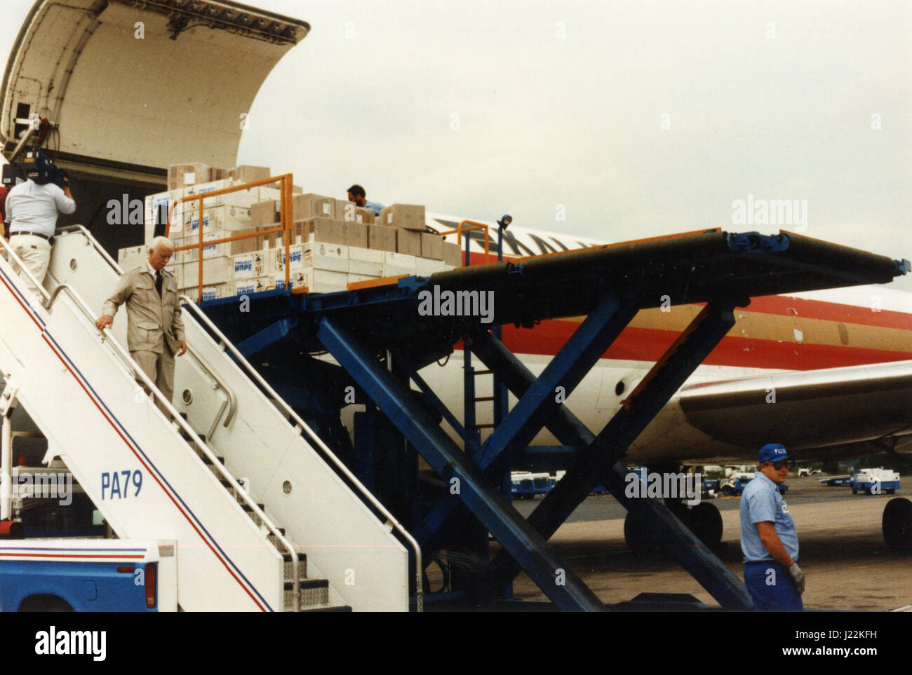 MAN WALKING DOWN THE STEPS OF AN AIRPLANE - BOXES OF CARGO BEING LOADED ...