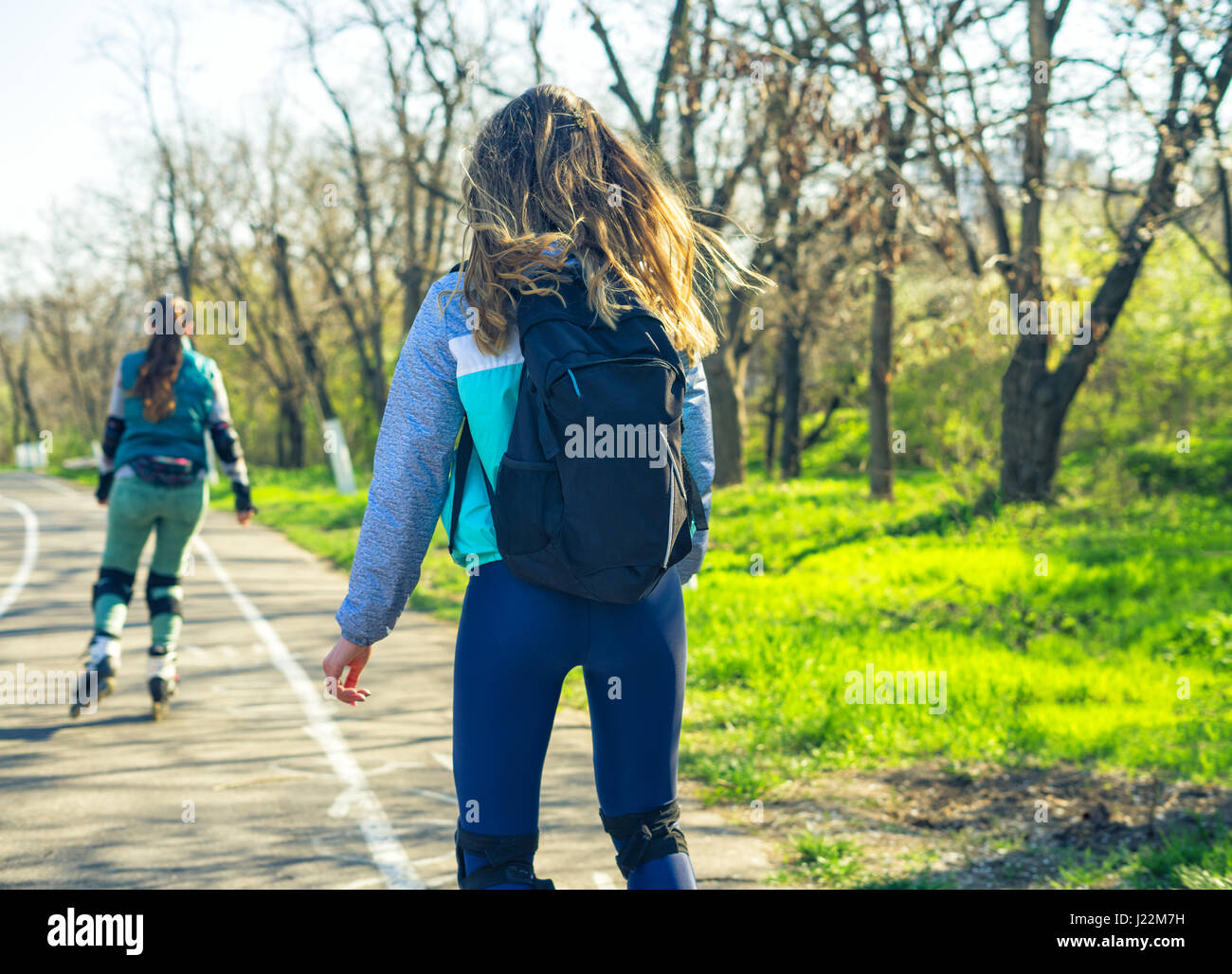 Two girls on roller skates ride along the road next to each other Stock ...