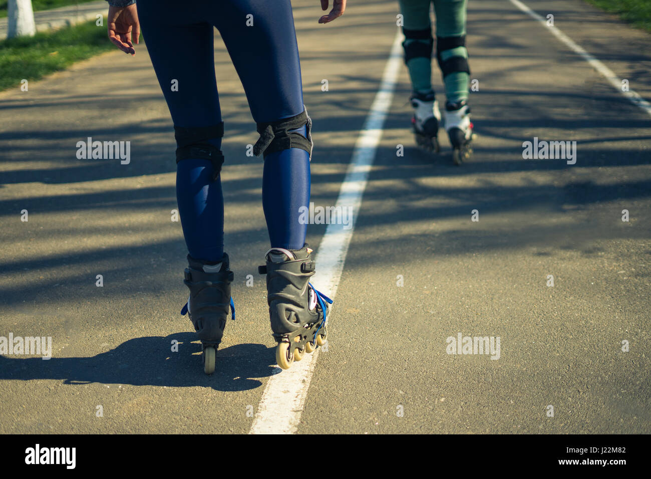 Two girls on roller skates ride along the road next to each other Stock ...