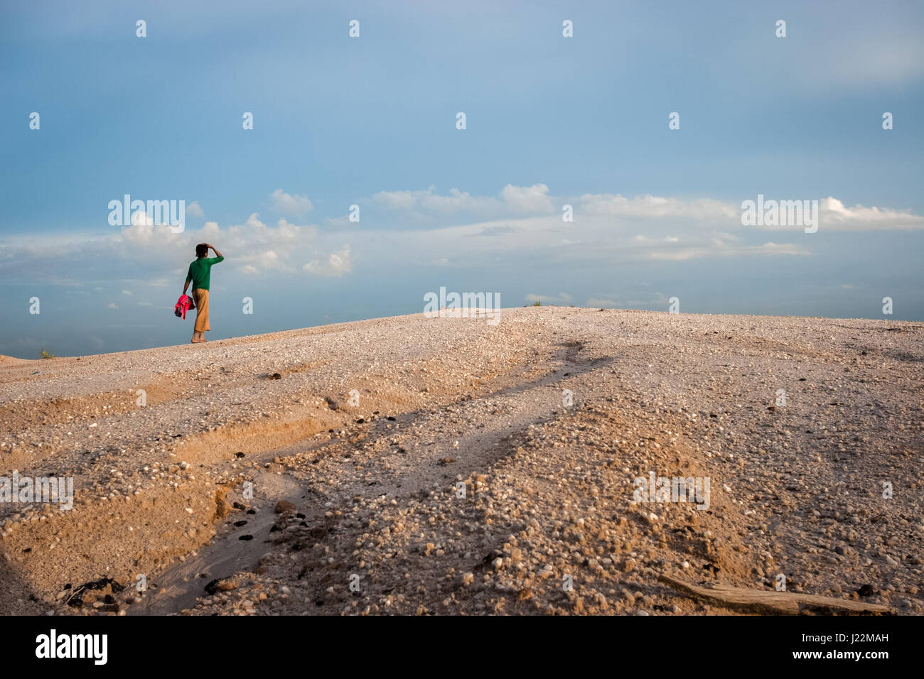 An unidentified gold miner walking on a sandy landscape where small ...