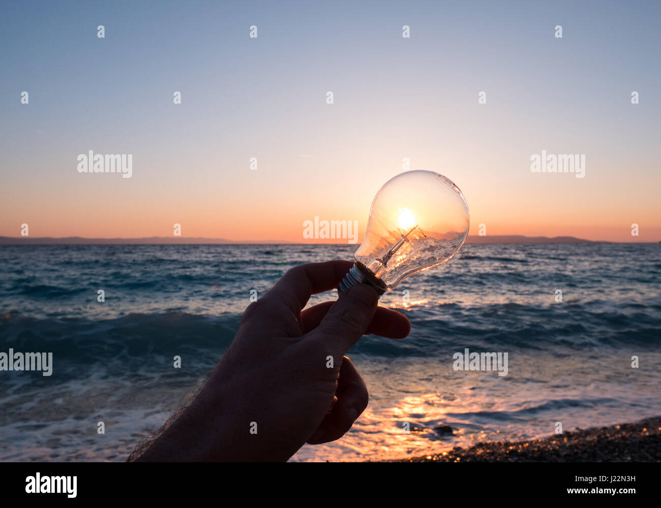 Man holding light bulb against sun on beach concept Stock Photo - Alamy