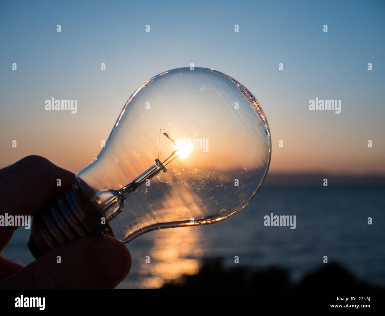 Man holding light bulb against sun at sunset Stock Photo - Alamy
