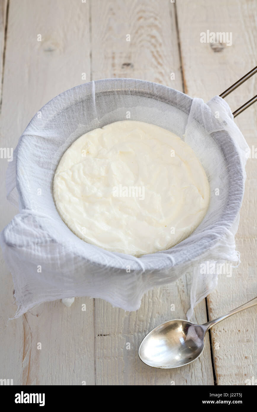 Straining yoghurt through muslin over a sieve, to make Greek style ...