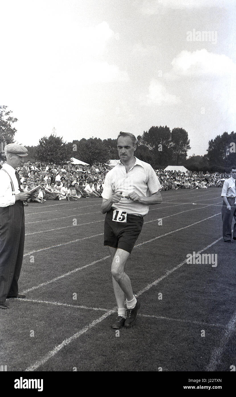 1950s, historical, male race walker hits the finishing tape at an ...