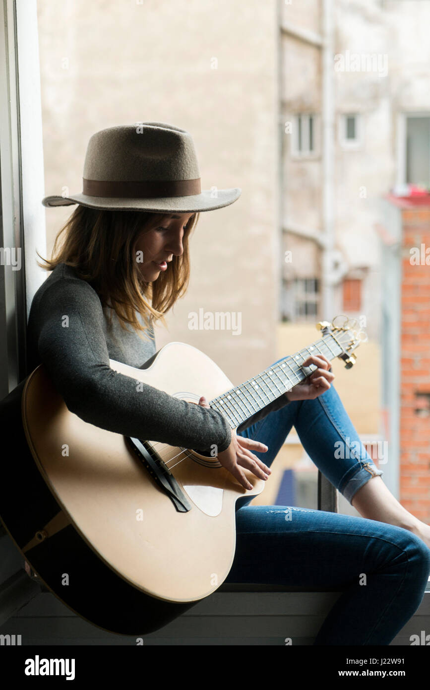 Young woman sitting in window frame playing guitar Stock Photo - Alamy