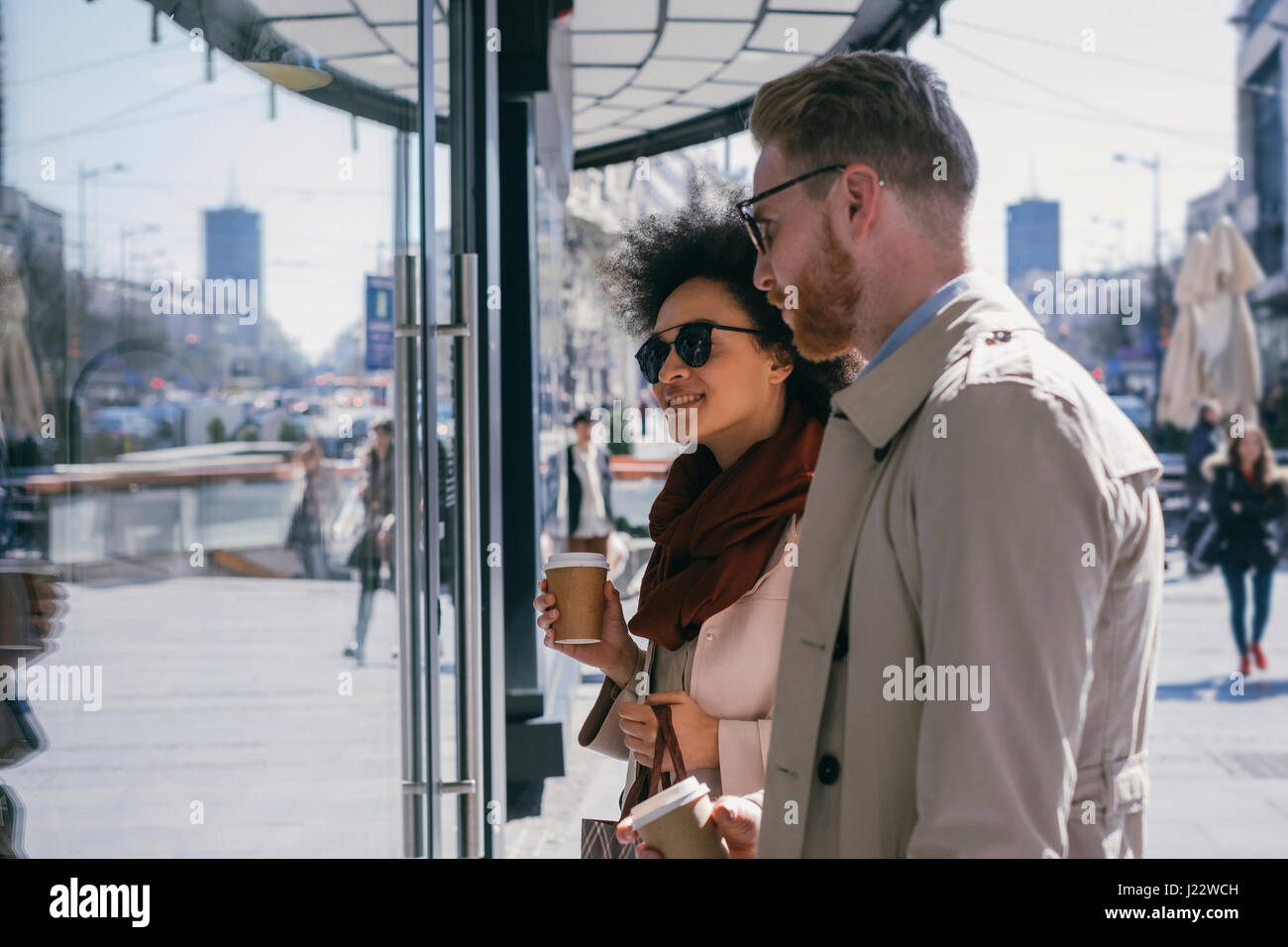 Couple in the city with takeaway coffee looking in shop window Stock ...