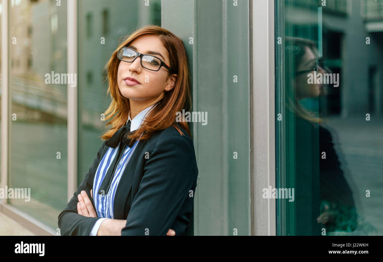 Businesswoman leaning against window with arms crossed Stock Photo - Alamy