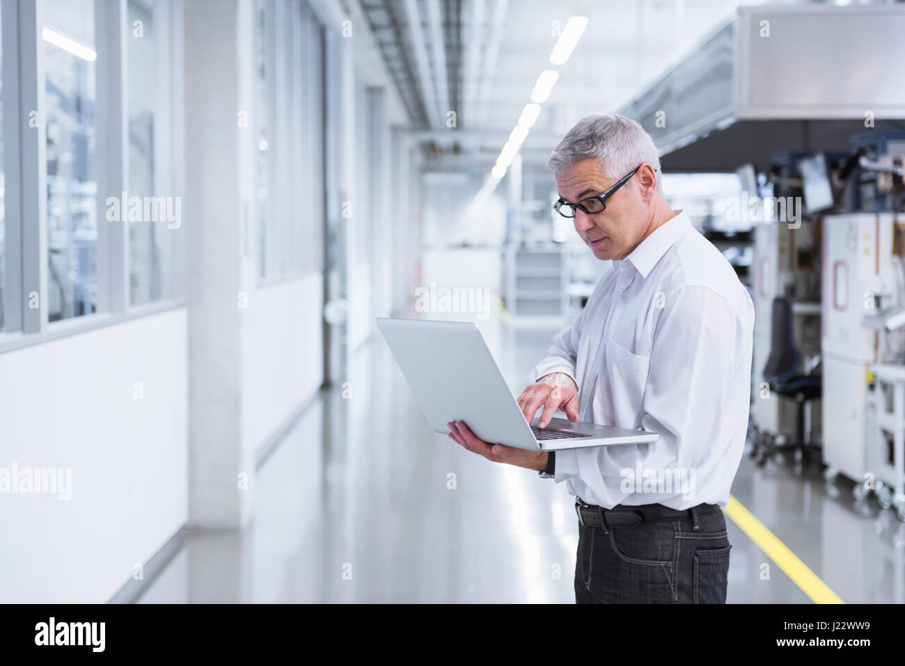 Manager on shop floor of a factory using laptop Stock Photo - Alamy