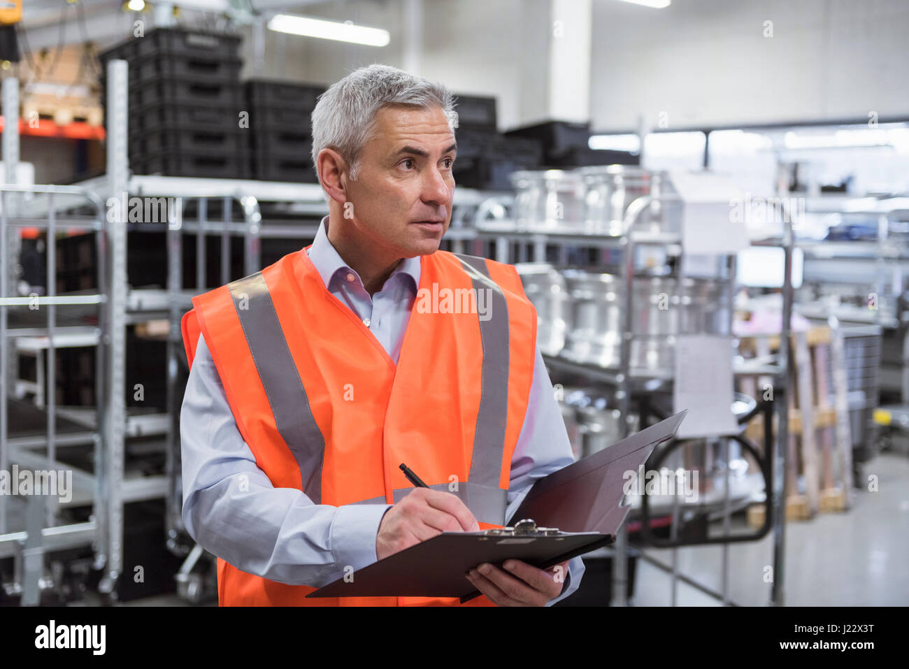 Man in factory hall wearing safety vest holding clipboard Stock Photo ...