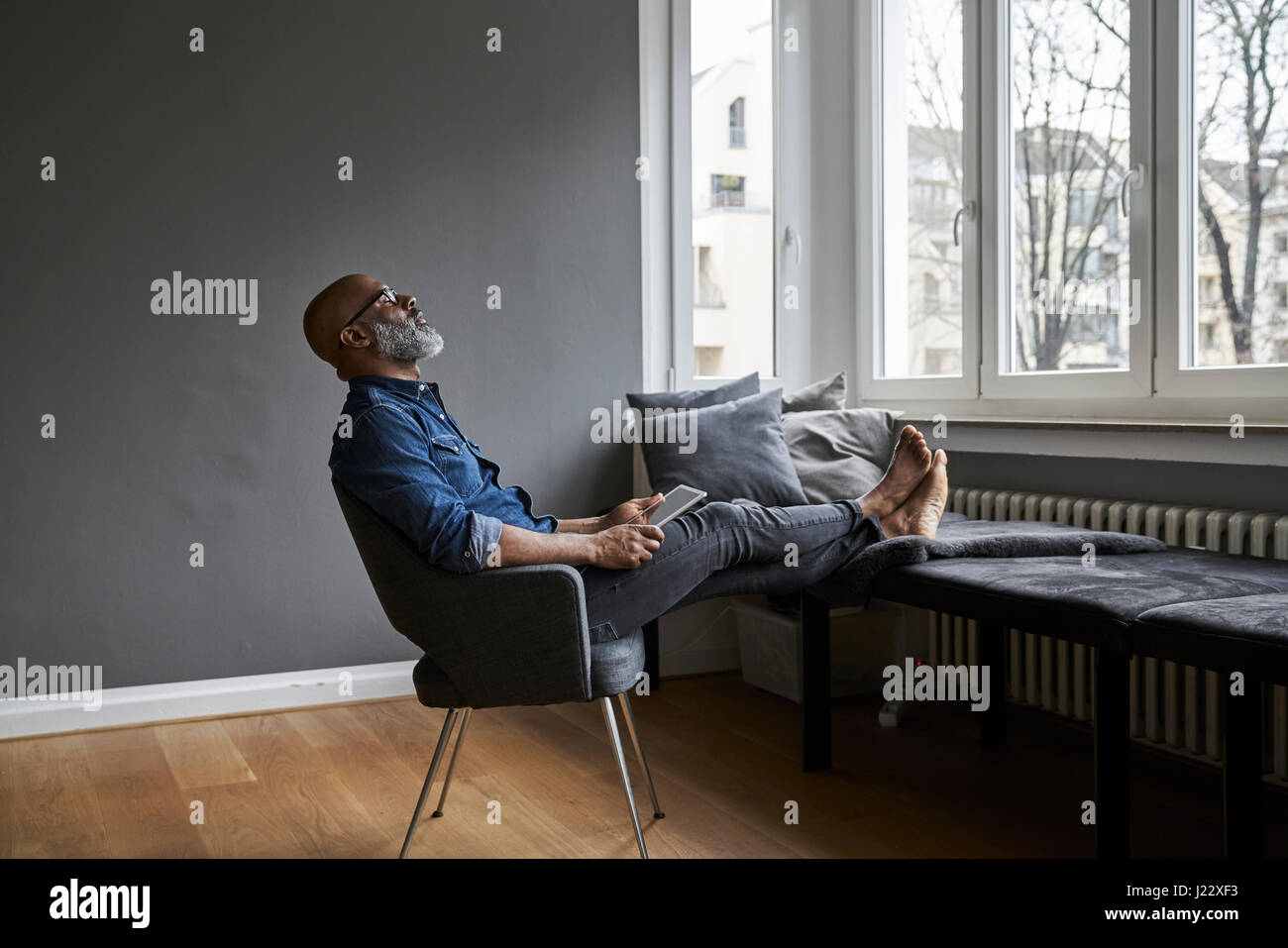 Man sitting with feet on bench, holding digital tablet Stock Photo - Alamy