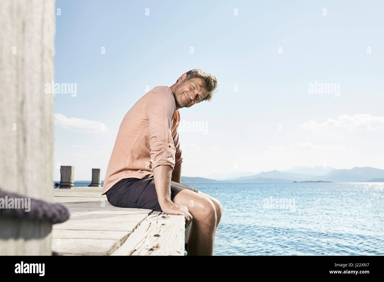 Smiling man sitting on jetty Stock Photo - Alamy