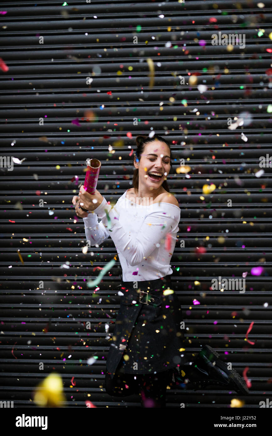 Happy young woman standing in front of black roller shutter throwing ...