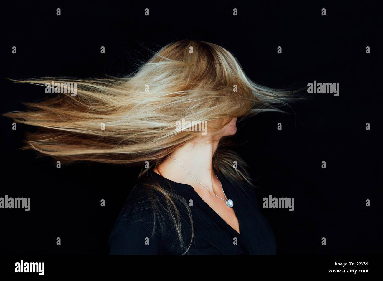 Young blond woman tossing her hair in front of black background Stock ...