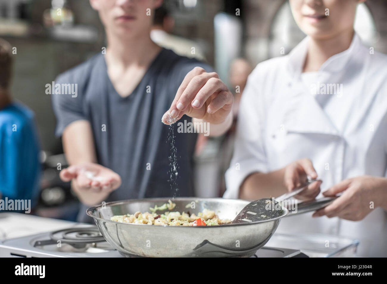 Teenager adding salt to pan Stock Photo - Alamy