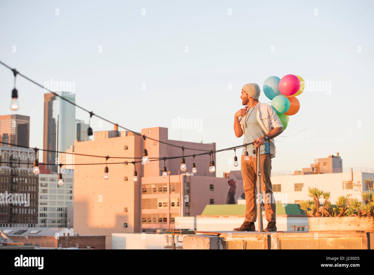 Young man standing on rooftop, holdng balloons Stock Photo - Alamy