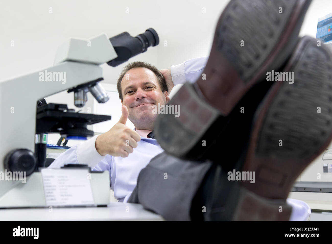 Successful doctor in a laboratory has his feet on the desk. Scientific ...
