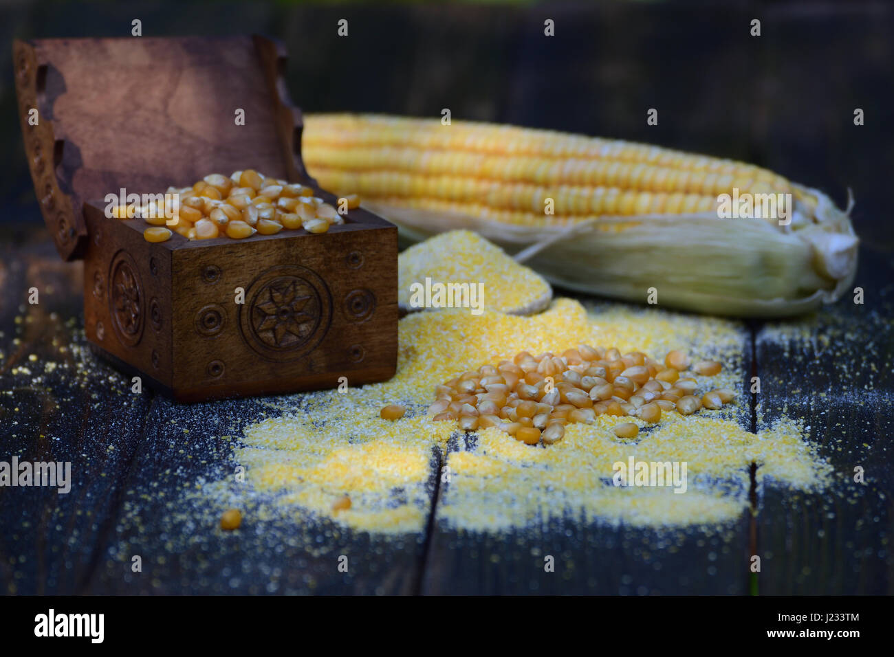A blurred corn cob placed next to a small wooden chest full of corn ...