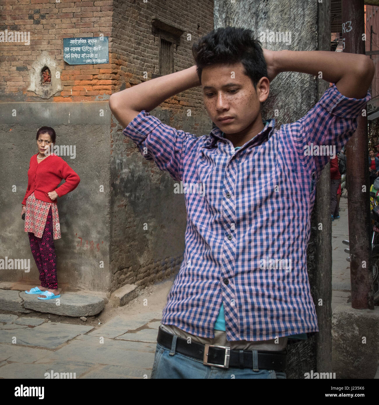 Teenage boy standing on the street as woman looks on in Patan, Nepal ...