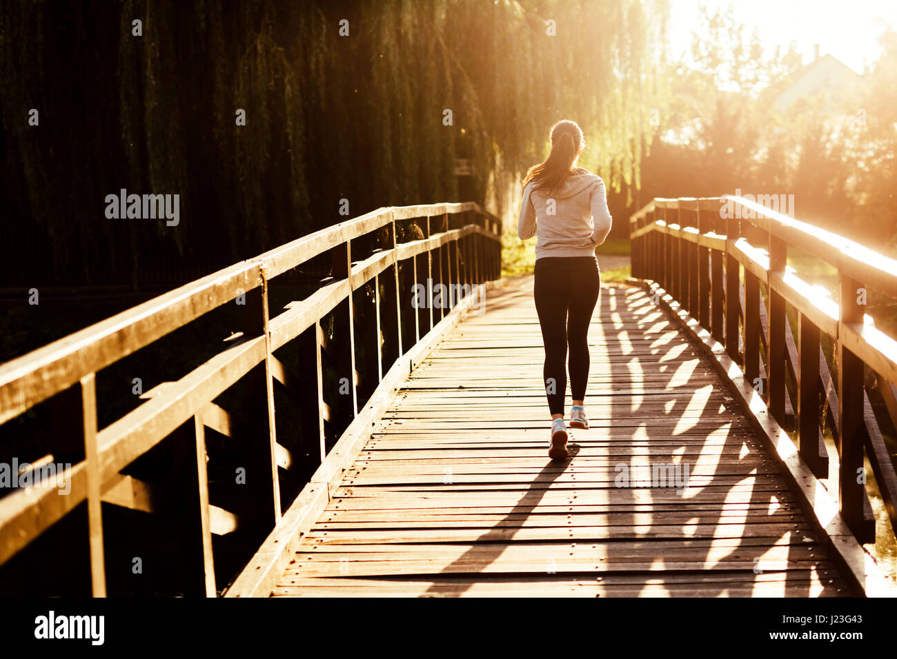 Beautiful female jogger running during sunset across bridge Stock Photo ...