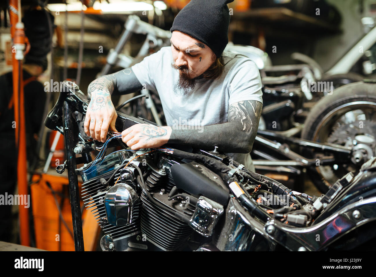 Portrait of modern heavily tattooed man assembling custom motorcycle in ...