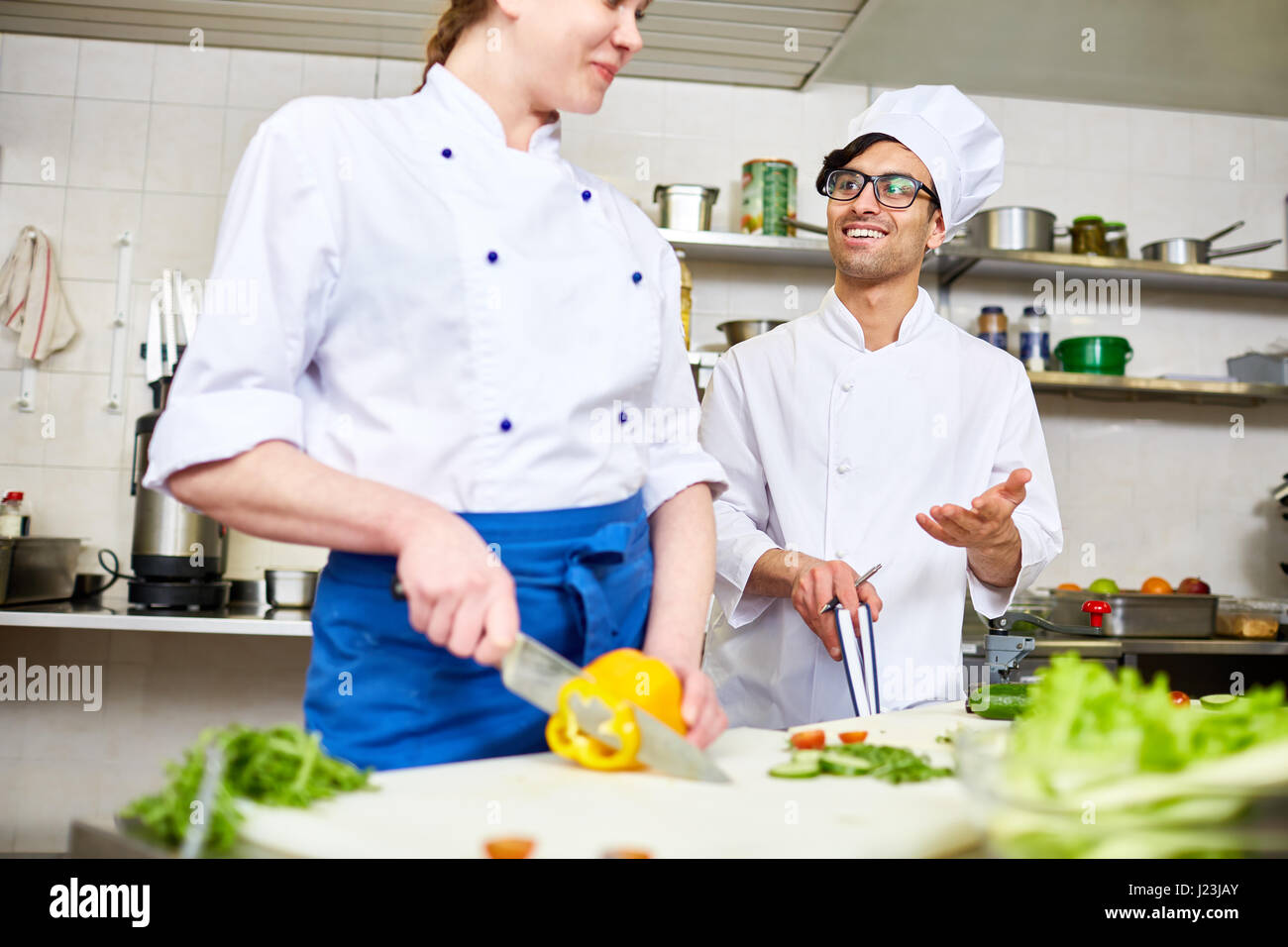 Contemporary chef in uniform consulting his trainee in the kitchen ...