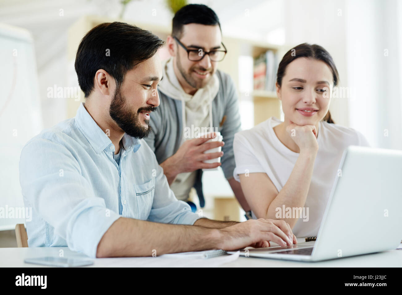 Group of smiling young business people looking at laptop screen in ...